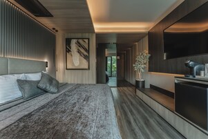 A modern hotel room with a large bed, a flat-screen TV, a built-in coffee machine, and a view of the outdoors.