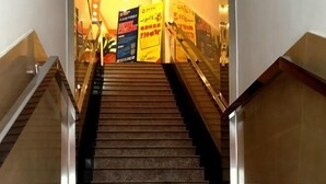 Uma escadaria com corrimãos, que leva a uma área bem iluminada com placas.