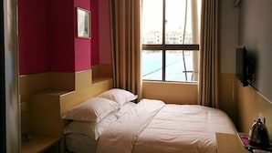 Quarto de hotel com cama, televisão, janela com cortinas e vista para prédios.
