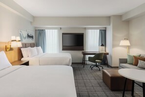 Quarto de hotel com duas camas, uma escrivaninha, televisão e área de estar.