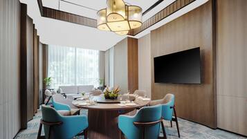 Uma sala de conferências moderna com uma mesa redonda, cadeiras azuis, um candelabro, uma TV de tela plana e uma janela grande com cortinas.