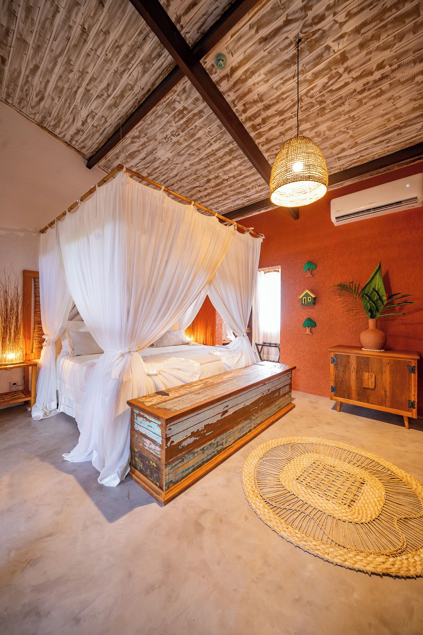 Quarto com cama, luminária pendente, ar condicionado fixado na parede e tapete tecido.