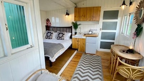 Quarto compacto e rústico em estilo cabana, com cama, pequena cozinha e área de jantar com móveis de vime.