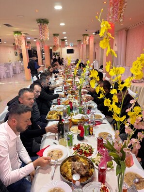 Uma longa mesa de jantar com várias pessoas sentadas, cercada por diversos pratos e bebidas.