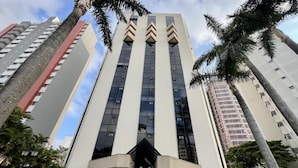 Um edifício alto com design moderno, rodeado por palmeiras e um jardim bem cuidado.