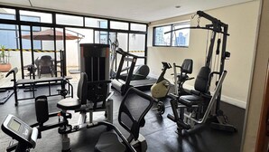 Uma academia com diversos equipamentos de exercício, janelas amplas e vista para a cidade.
