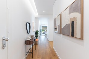 Um corredor com piso de madeira, porta com puxador moderno, pequena mesa com objetos decorativos e arte abstrata na parede.