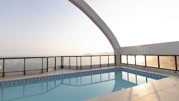Piscina com vista clara para o mar e montanhas ao longe.