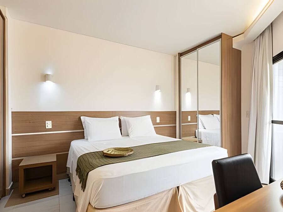 Quarto de hotel com cama, mesas de cabeceira, escrivaninha e uma cadeira.