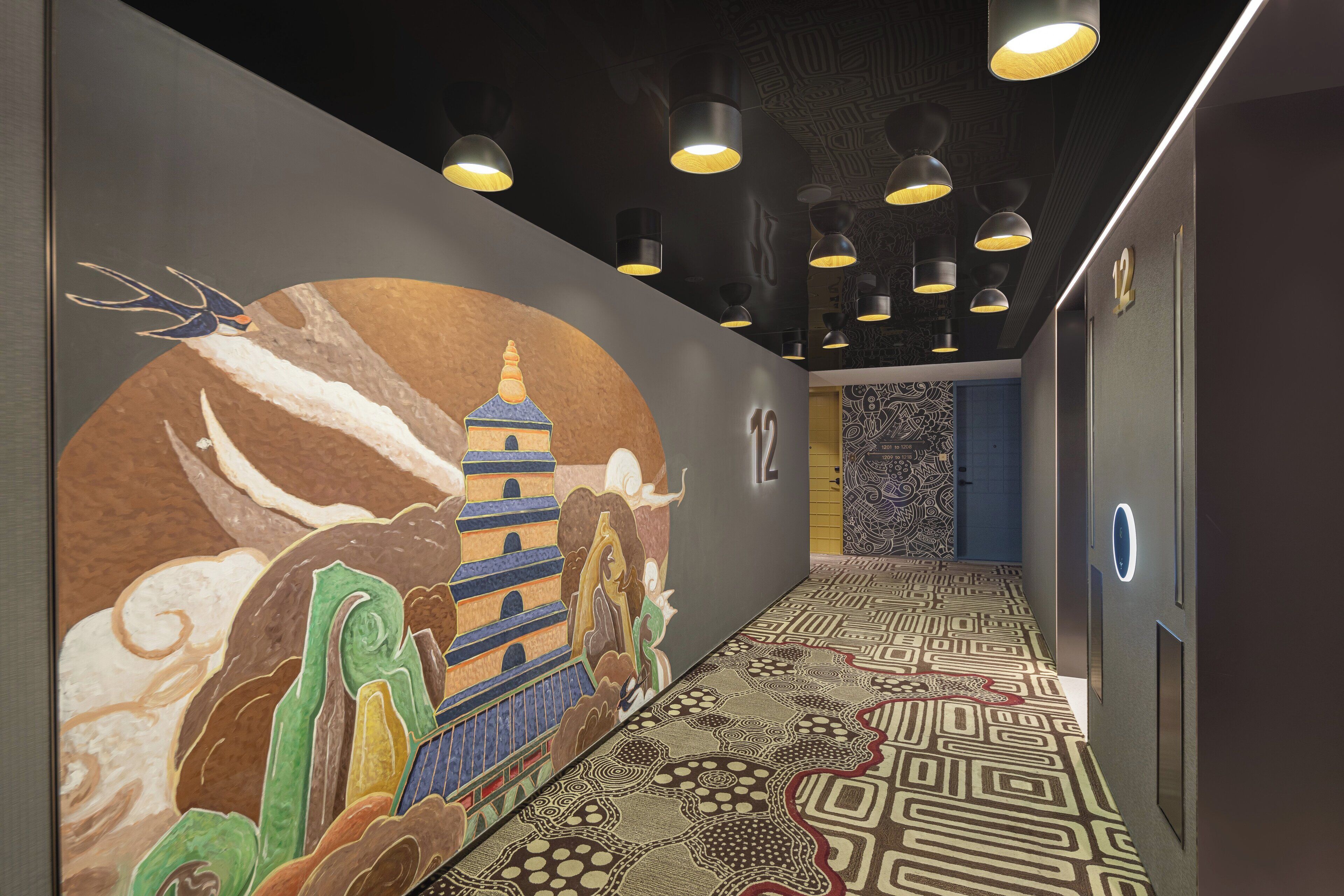 Um corredor com um mural, carpete estampado e luminárias modernas.