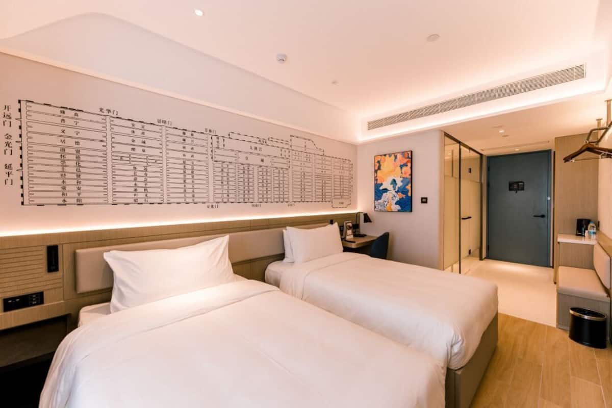 Quarto de hotel com duas camas, um mapa de parede grande, um quadro e um banheiro visível por uma porta aberta.