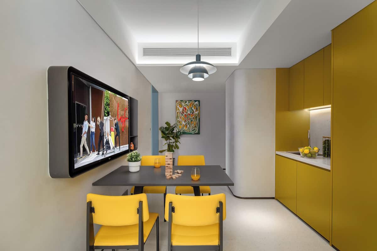 Uma sala de jantar moderna com uma mesa preta, cadeiras amarelas, uma grande televisão de tela plana e uma cozinha com armários amarelos.