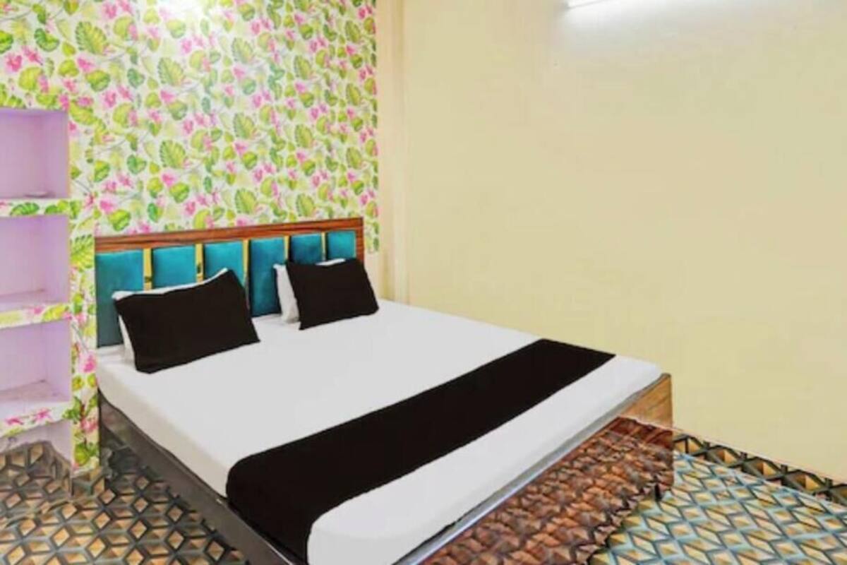 Uma cama com colchão branco e colcha preta, cabeceira com almofadas verde-água e papel de parede estampado com flores.