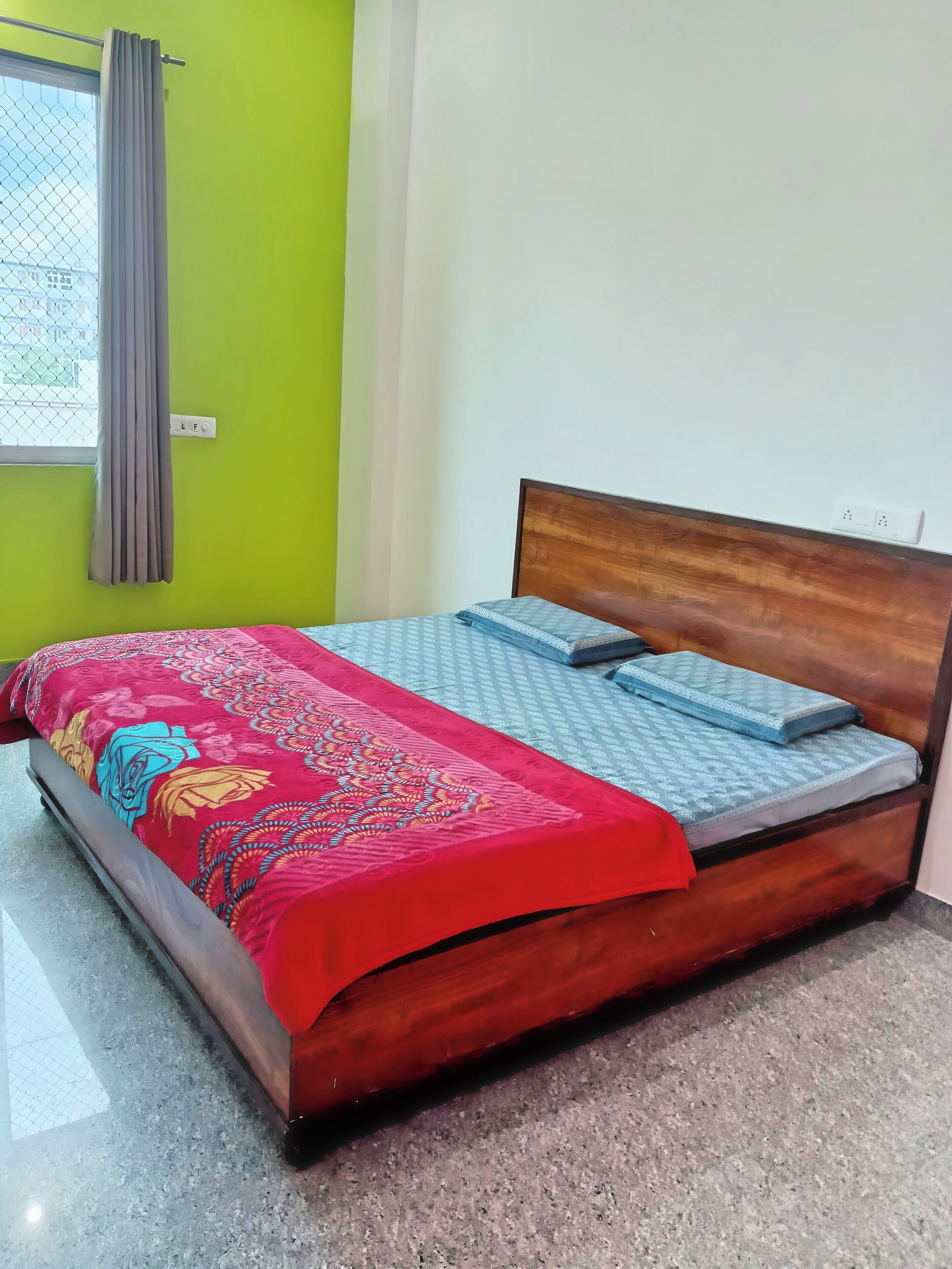 Uma cama com cabeceira de madeira, colcha estampada e janela com cortinas.