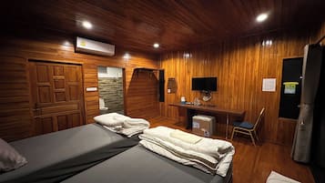 Quarto com painéis de madeira, duas camas, uma escrivaninha, televisão e ar condicionado.