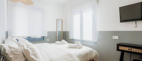 Quarto de hotel moderno com cama, escrivaninha, televisão e uma janela grande.