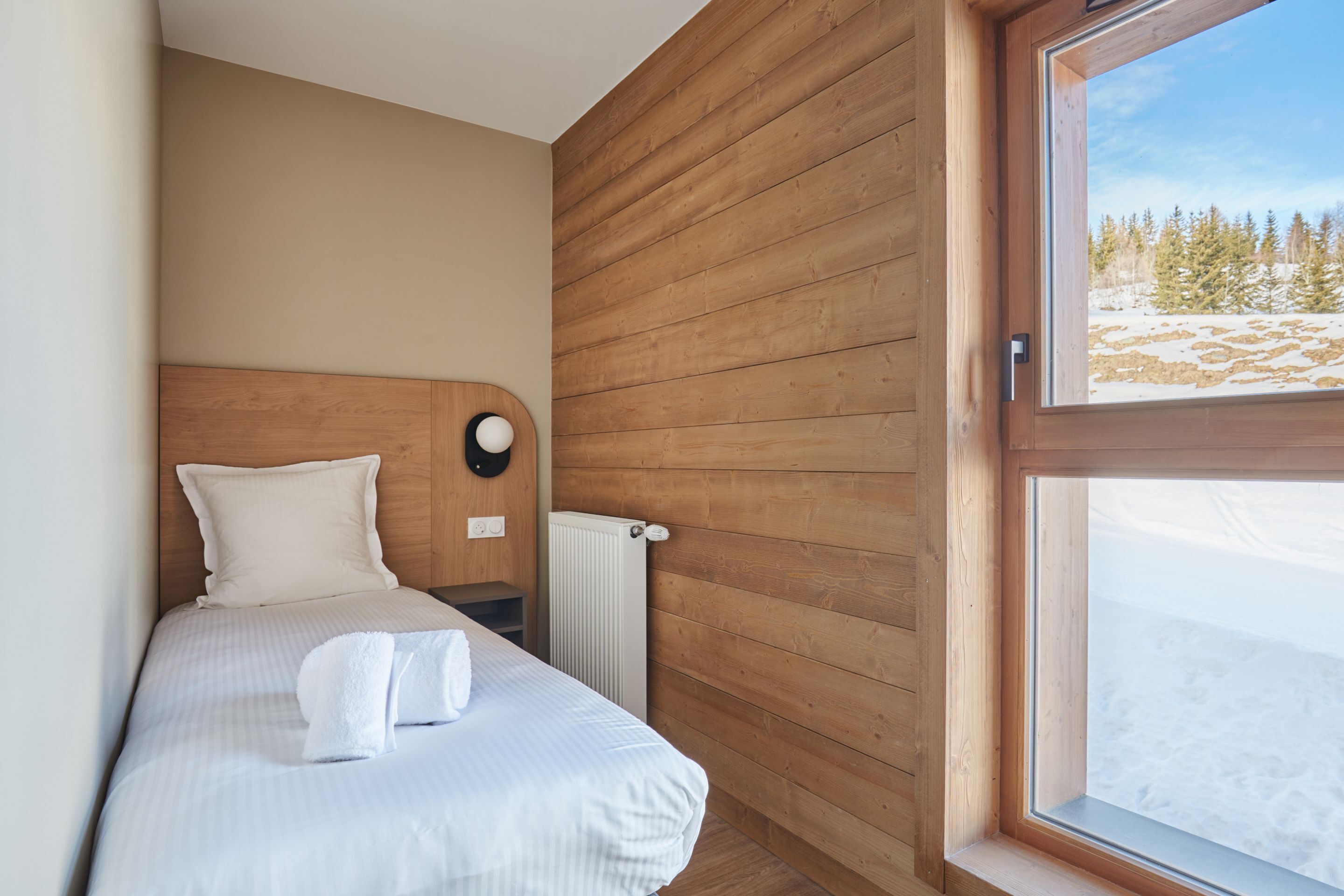 Quarto com cabeceira de madeira, janela com vista para uma paisagem nevada e radiador.