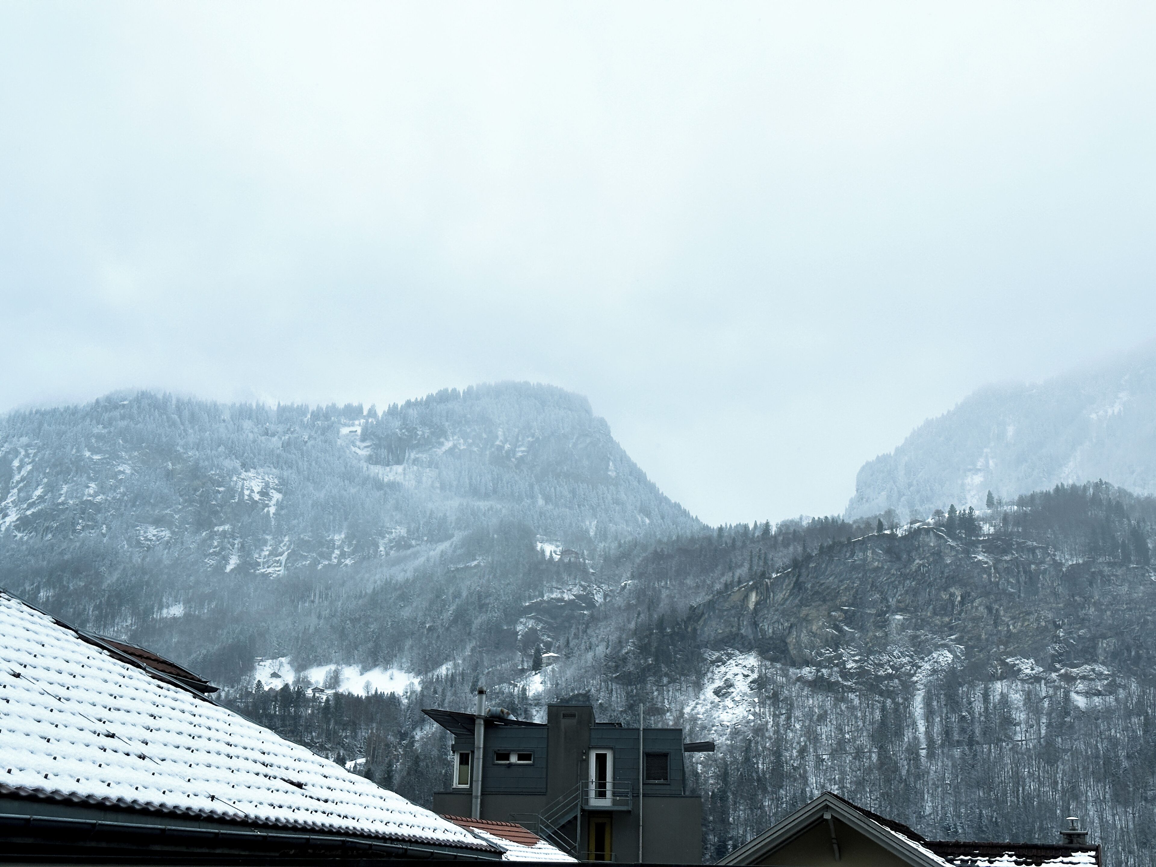 Paisagem montanhosa com picos cobertos de neve e um edifício com telhado inclinado.