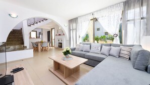 Uma sala de estar moderna com um sofá cinza, mesa de centro de madeira e uma escada para um andar superior.