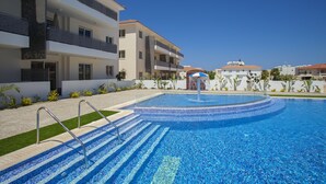 Um hotel moderno com piscina, várias varandas e um céu azul límpido.
