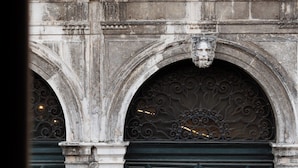 Fachada de um edifício histórico com duas grandes portas verdes, um arco de pedra decorativo e uma varanda com guarda-corpos de madeira.