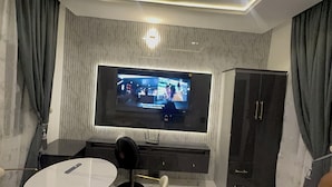Uma sala de estar moderna com uma televisão de tela plana na parede, um rack de entretenimento preto, uma mesa de centro redonda de vidro e um sofá preto.