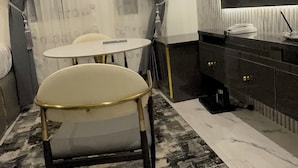 Uma sala de estar moderna com uma mesa redonda e uma única cadeira, uma TV de tela plana na parede e um armário escuro com um telefone e controle remoto em cima.