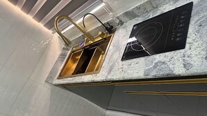 Cozinha com bancada de granito, torneira dourada e fogão por indução preto.