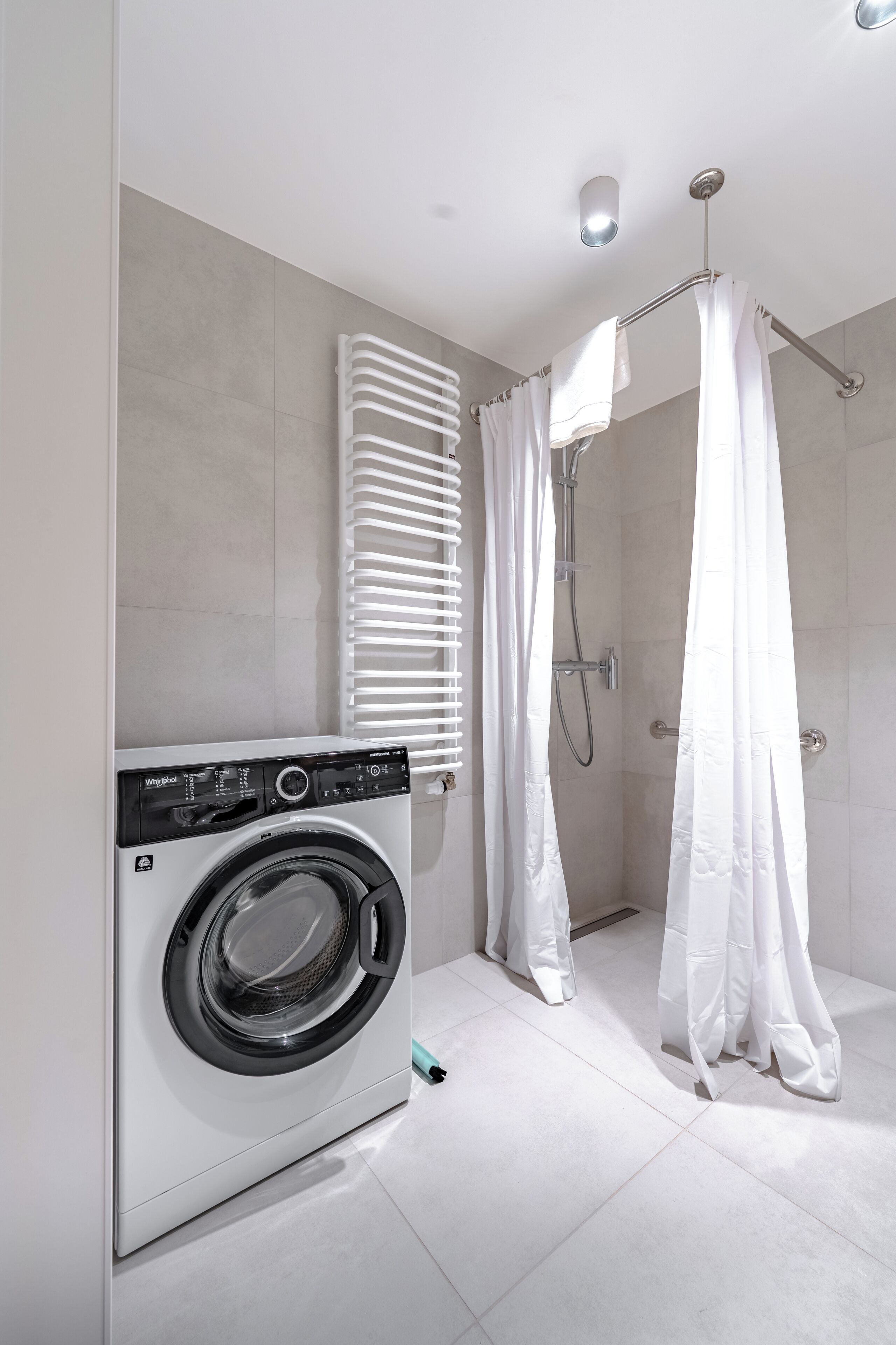 Uma casa de banho moderna com máquina de lavar frontal, chuveiro com porta de vidro e porta-toalhas.