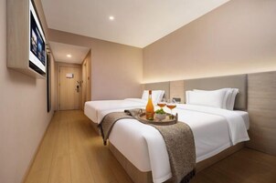Quarto de hotel com duas camas, piso de madeira, televisão fixada na parede e um recipiente com garrafa e copos sobre a cama.