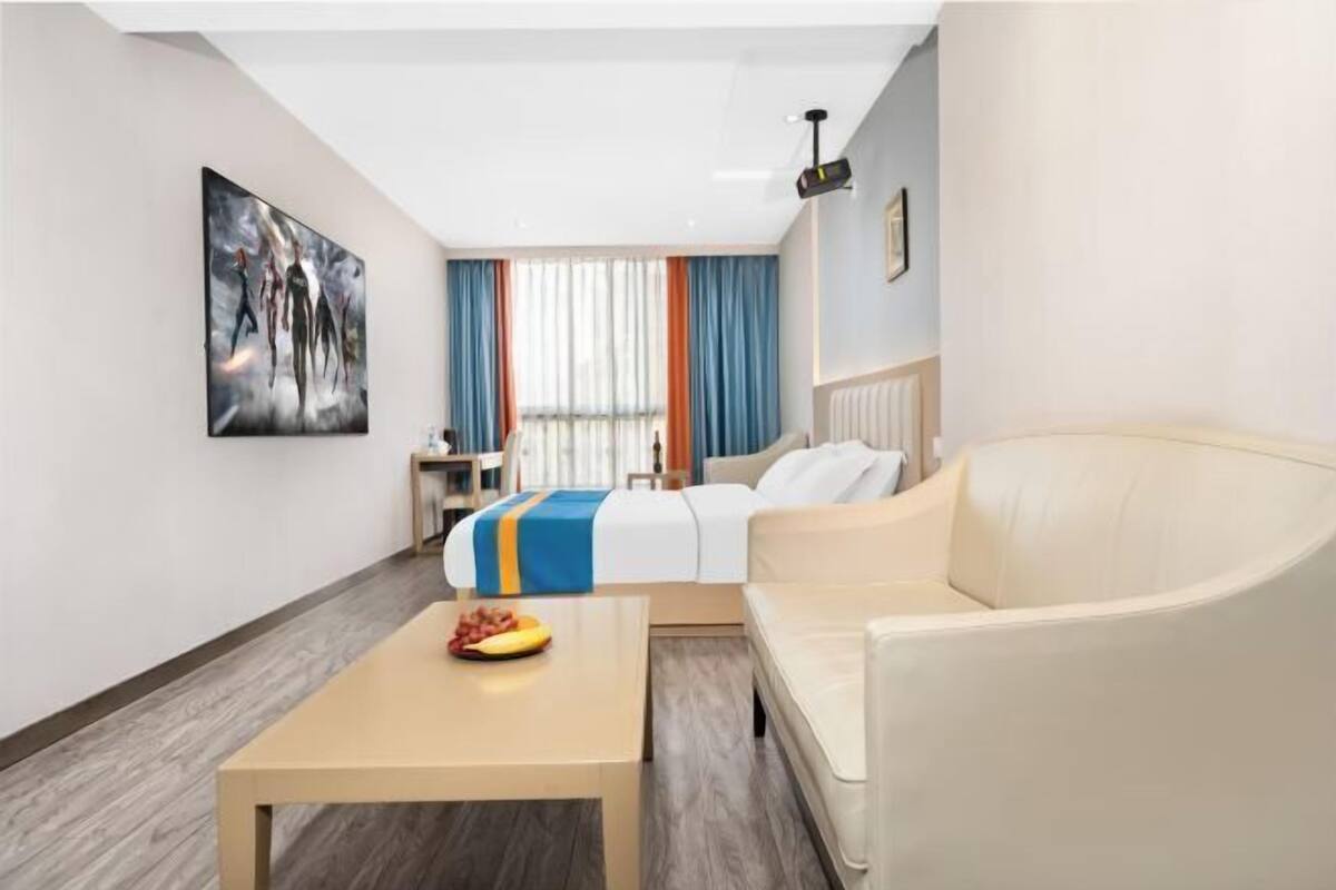Quarto de hotel com cama, sofá, mesa de centro e um quadro na parede.
