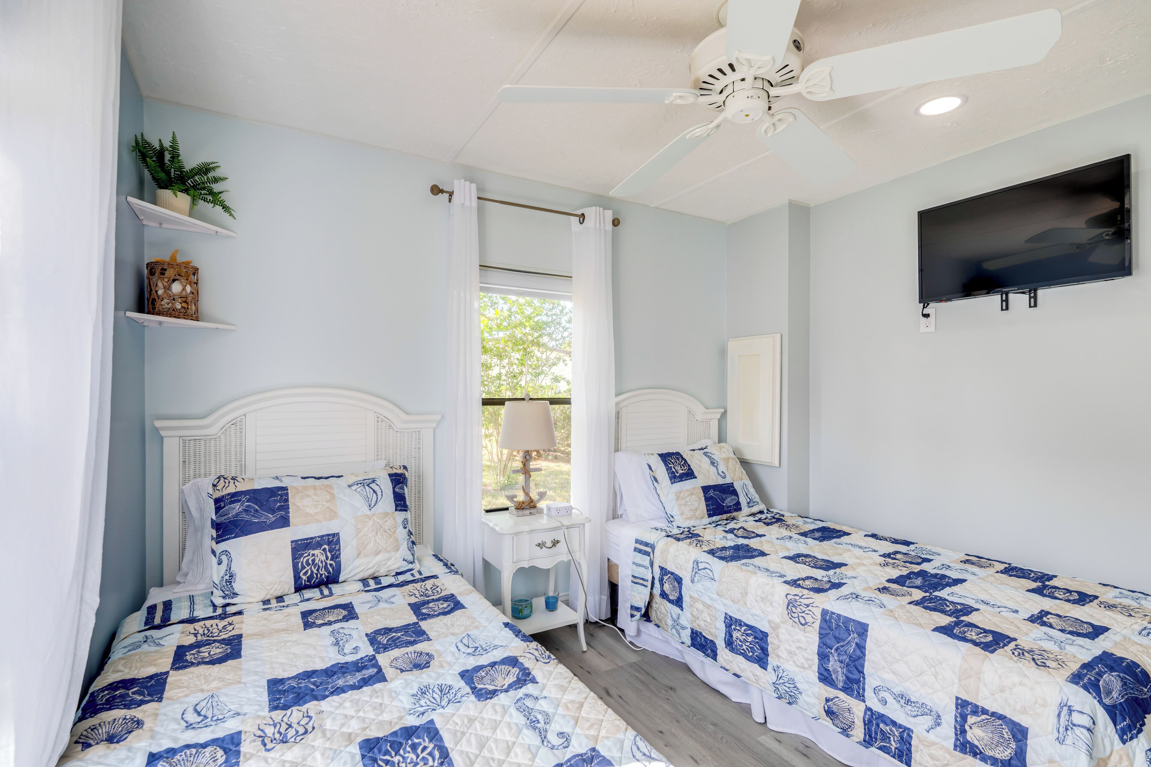 Quarto com duas camas, um ventilador de teto, uma televisão e uma janela com cortinas.