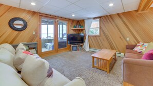 Uma sala de estar aconchegante com teto de madeira, TV de tela plana, sofá, mesa de centro e estante.