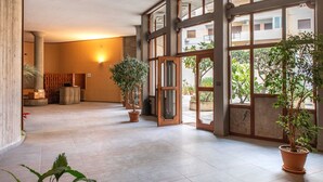 Um hall amplo com teto alto, janelas grandes e plantas em vasos.