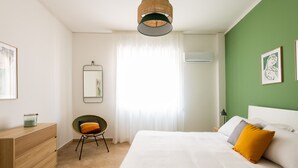 Quarto com cama, cómoda de madeira, cadeira e janela com cortinas.