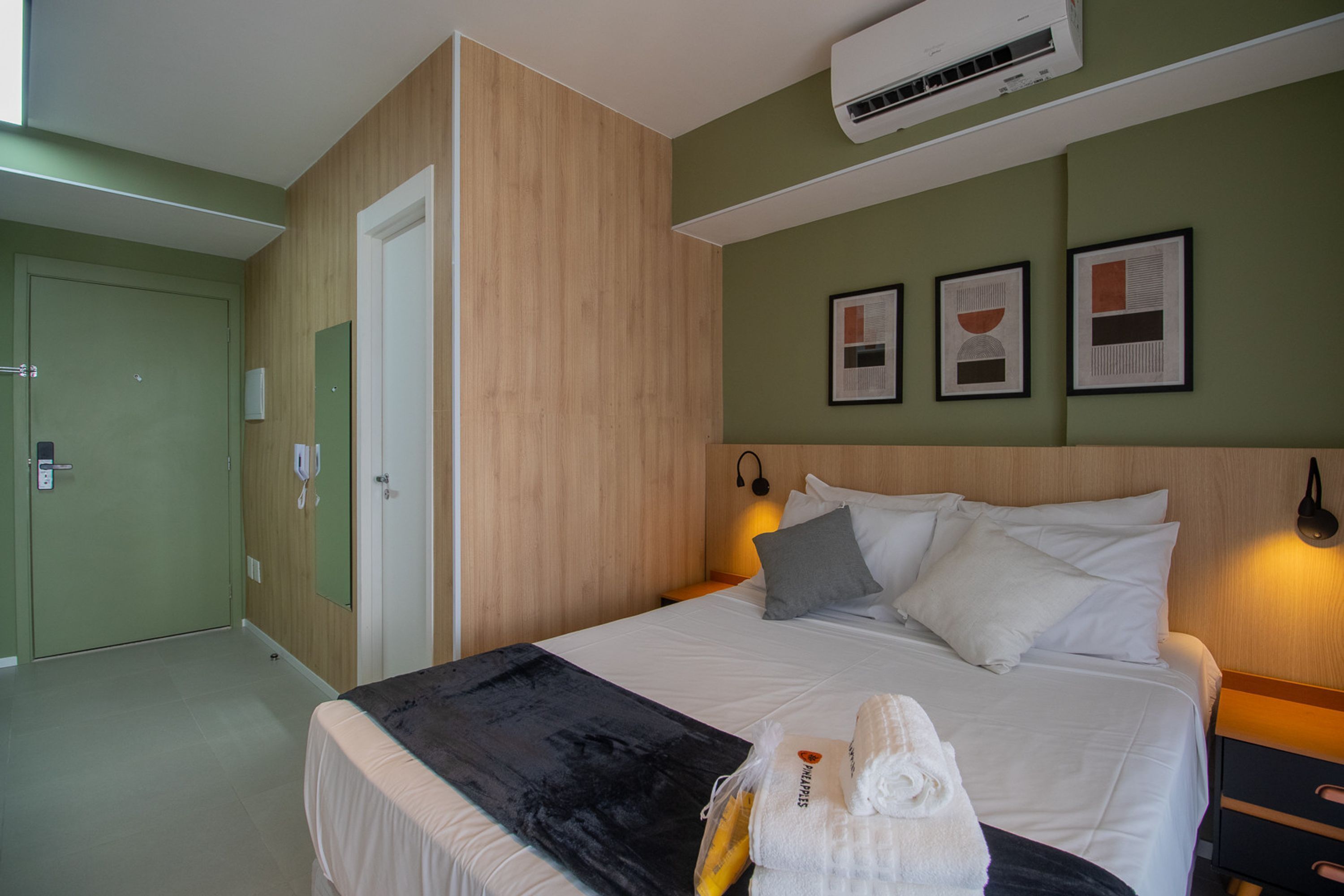 Quarto de hotel com cama, mesa de cabeceira, telefone fixado na parede e ar condicionado na parede.