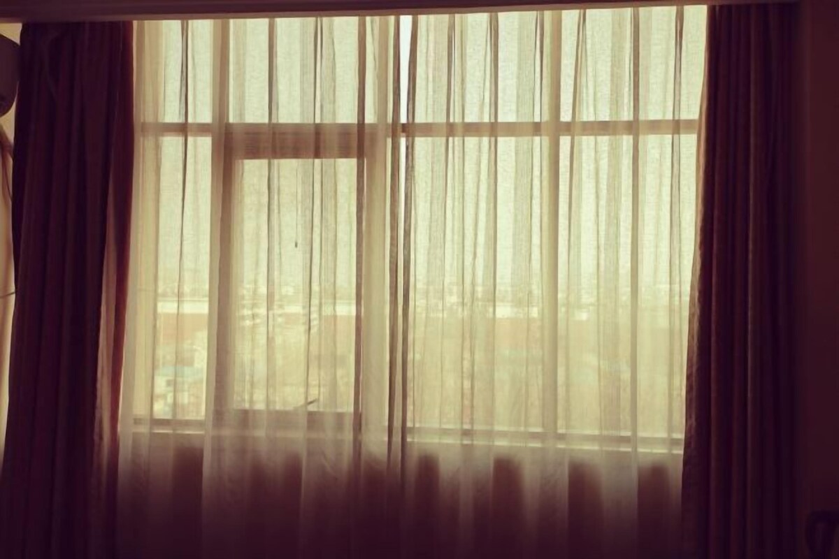 Um quarto com uma janela grande coberta por cortinas leves, permitindo a entrada de luz natural.