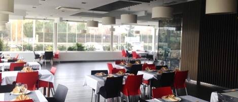 Um restaurante com mesas e cadeiras, grandes janelas e vista para o exterior.