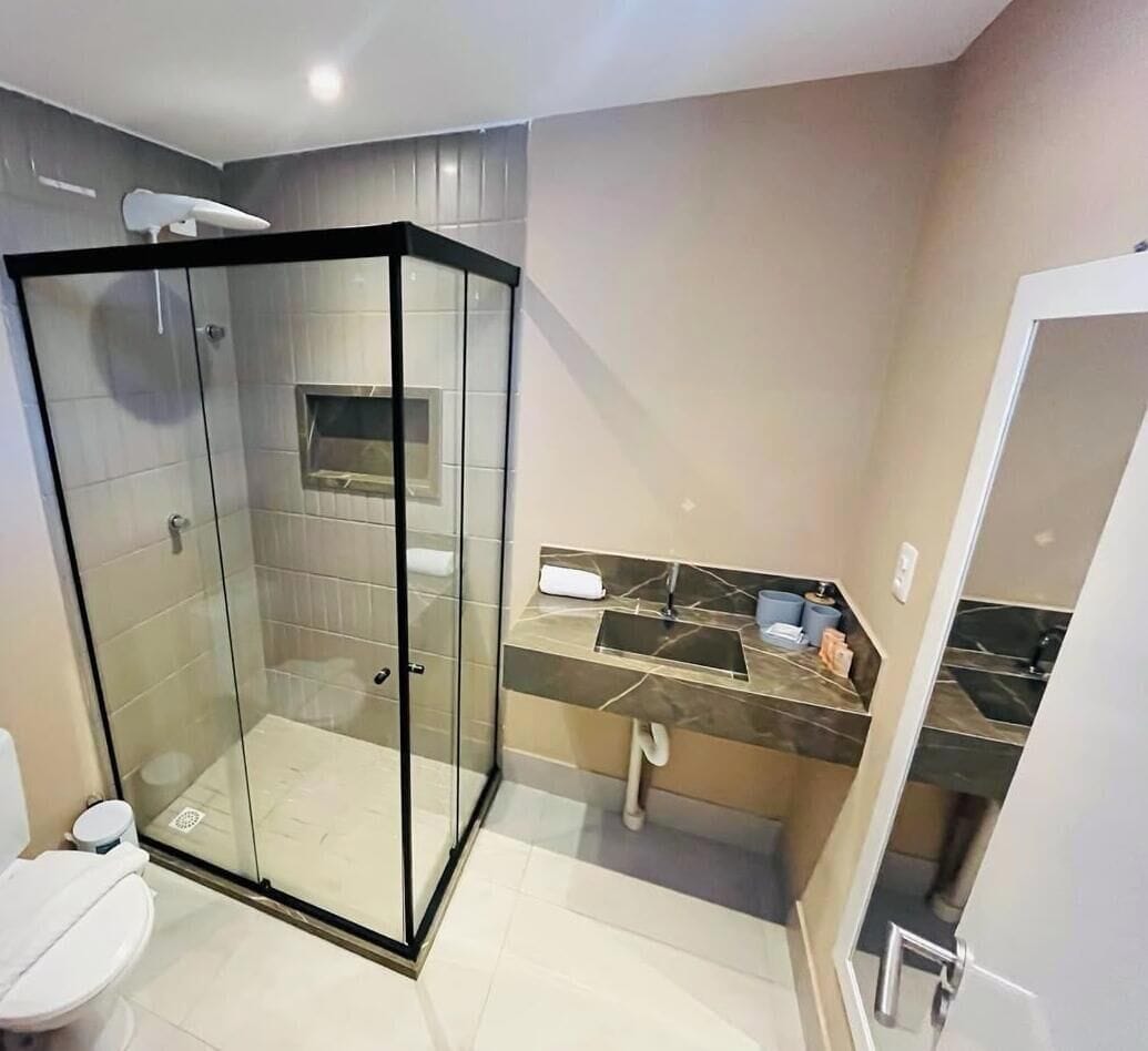 Uma casa de banho moderna com chuveiro em cabine de vidro, sanita e toucador com lavatório e bancada.