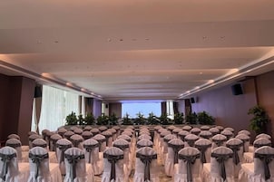 Sala de conferência com fileiras de cadeiras, cada uma com toalha branca e laço cinza.
