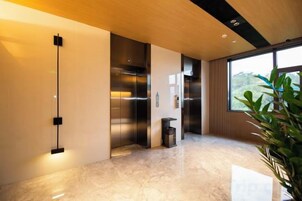Elevador moderno com acabamento metálico, piso de mármore e uma grande janela com vista para o verde lá fora.