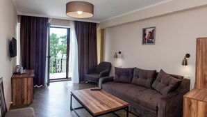 Uma sala de estar moderna com um sofá, uma mesa de centro de madeira, uma poltrona e uma televisão. Há uma porta que dá para uma varanda com cortinas.