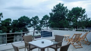 Terraço com móveis de vime, uma mesa de vidro e vista para árvores e edifícios.