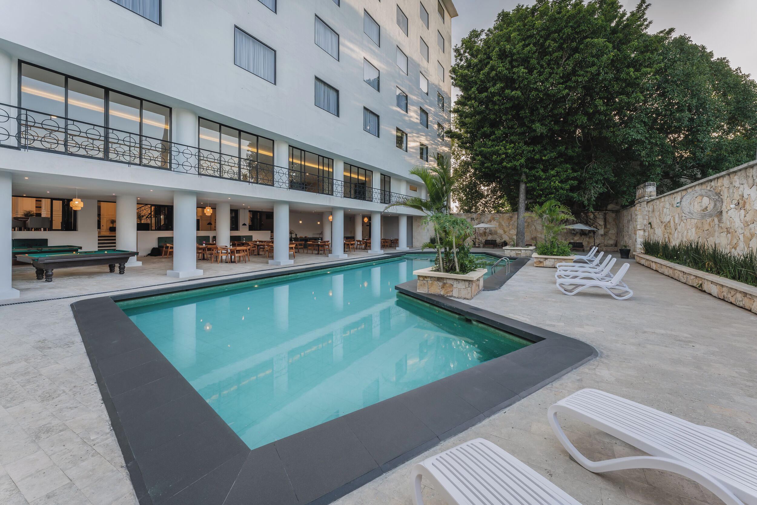Uma área de piscina com espreguiçadeiras, uma piscina e um edifício com vários andares e varandas.