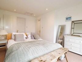 Quarto com cama, mesa de cabeceira, abajur, cômoda, espelho e um banco.