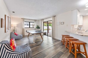 Uma sala de estar moderna com mesa de pingue-pongue, cadeiras de poltronas tipo bean bag listradas e banquinhos de madeira.