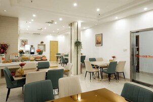 Uma área de refeições de hotel com mesas, cadeiras, um balcão de recepção e uma grande janela.