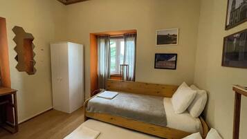 Quarto com duas camas, um guarda-roupa e uma janela com cortinas.