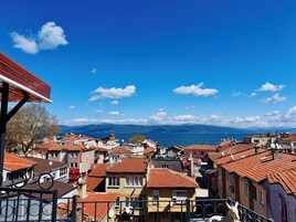 Uma vila costeira com telhados vermelhos e vista para o mar e montanhas ao longe.