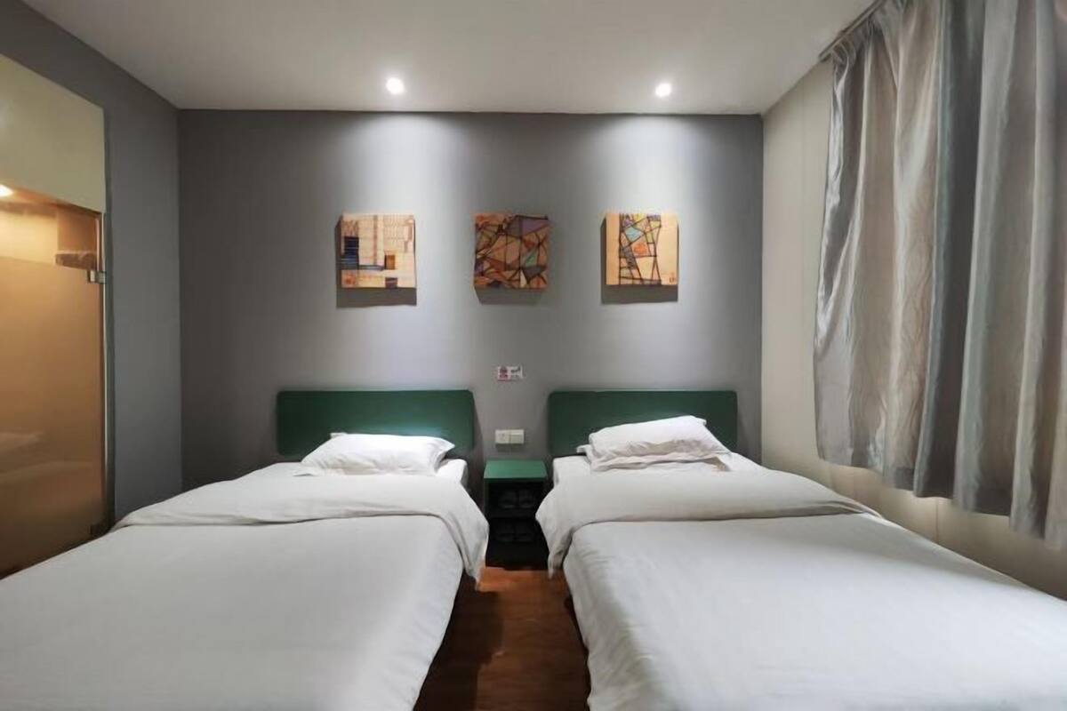 Quarto de hotel com duas camas, uma obra de arte na parede, janela com cortinas e piso de madeira.